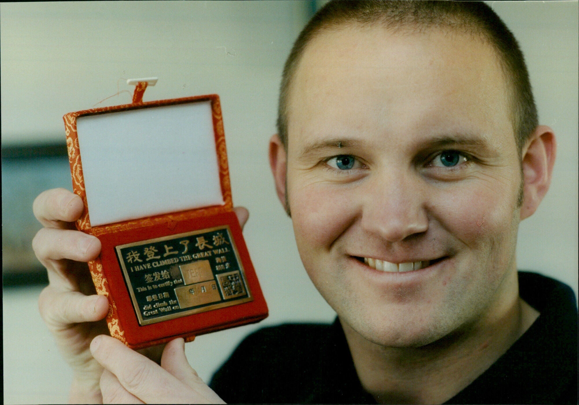 Geoff Jeff Batten stands atop the Great Wall of China with a plaque ce