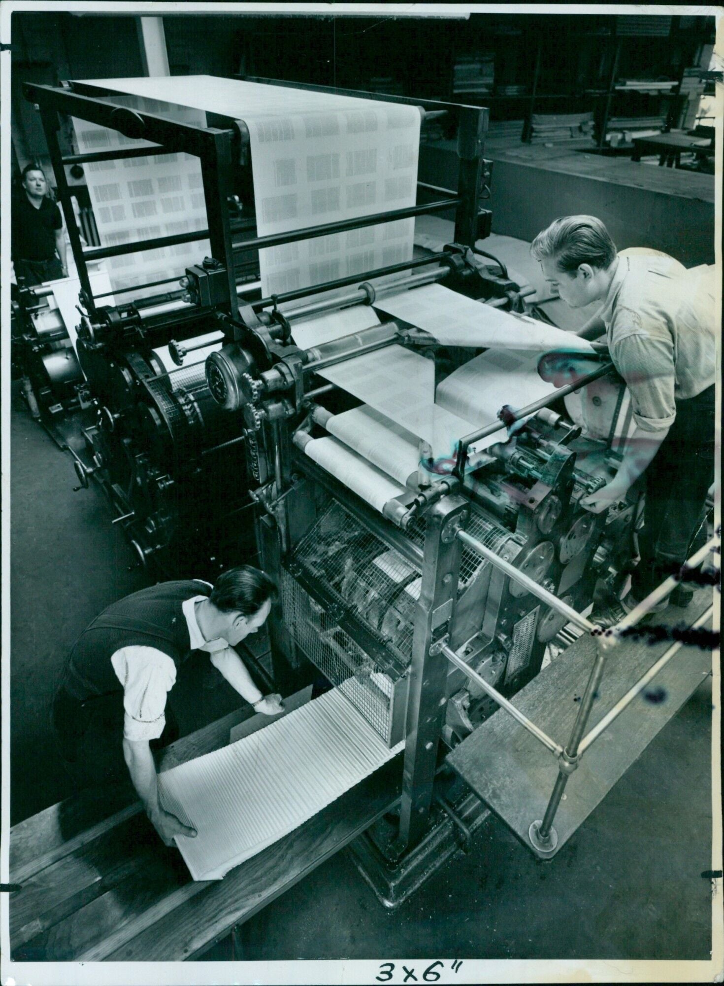 An assistant worker tends to a rotary printing press at a factory. - V